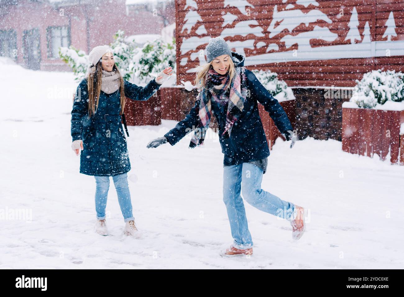 Two young women play snowballs and laugh while walking through a snowy ...
