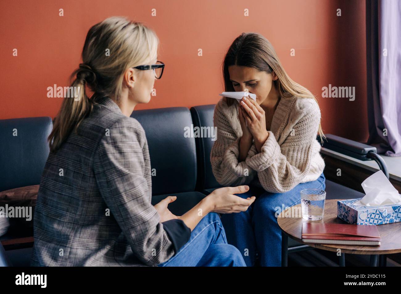 Female patient sitting on sofa and crying while psychotherapist ...