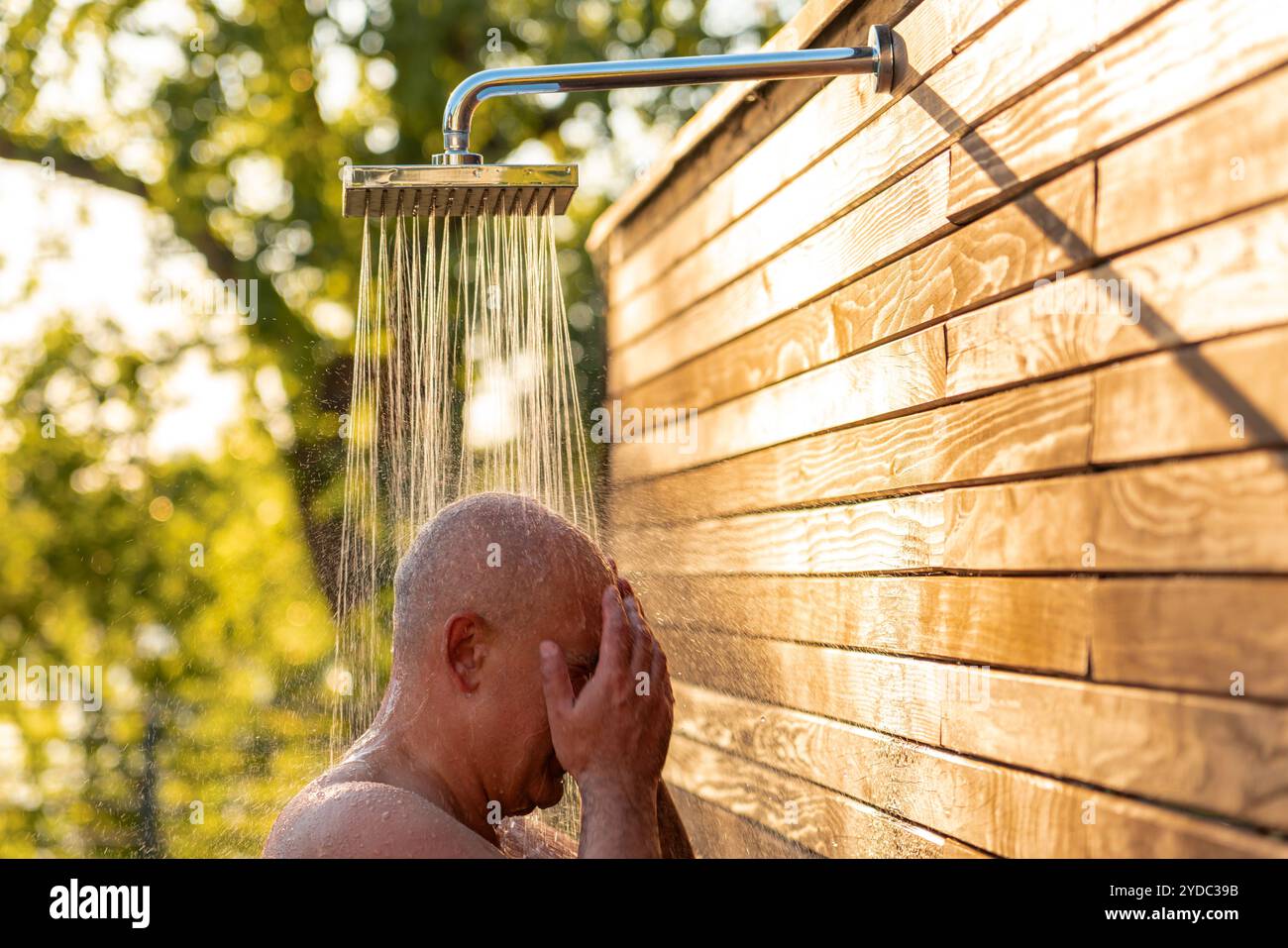 Man standing under outdoor shower at sunset, enjoying a refreshing ...