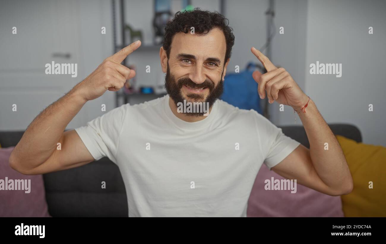 A smiling bearded man in a white shirt making finger guns at his head ...