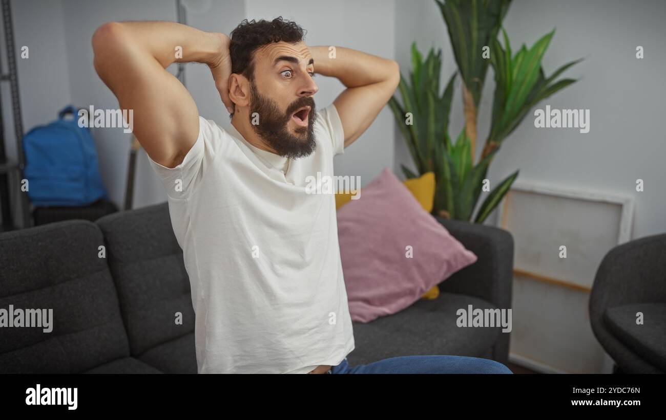 Surprised man with beard sitting indoors on a couch, expressing shock ...