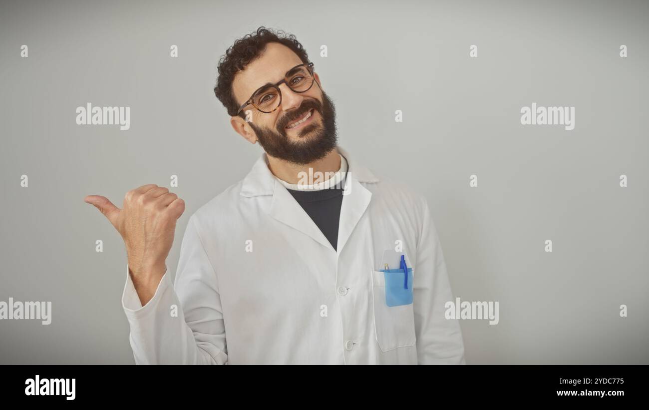 Smiling bearded man in lab coat pointing sideways against a white ...