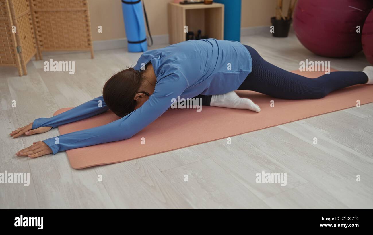 Woman stretching indoors on a mat in a gymnasium wearing blue ...