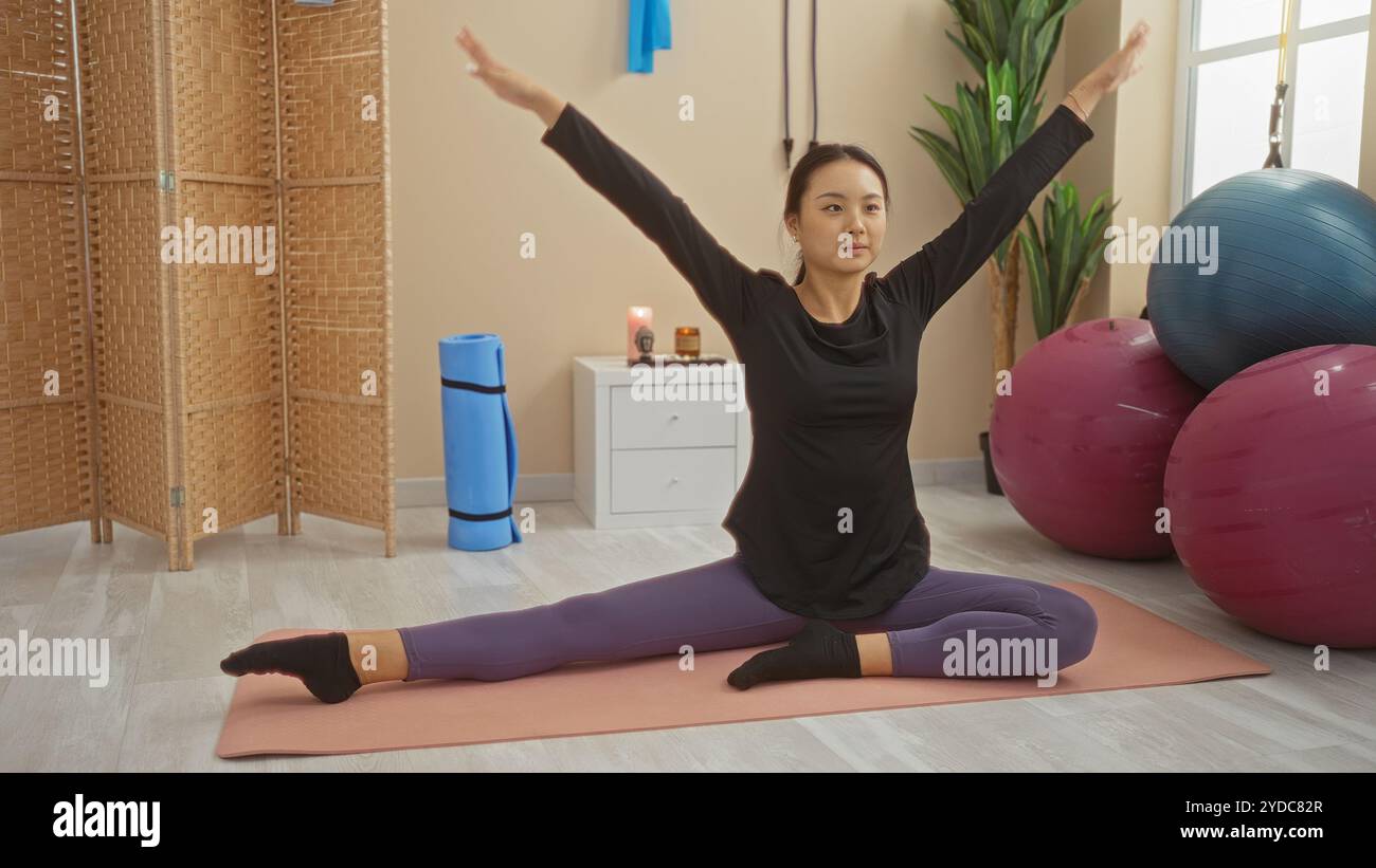 Young chinese woman practicing yoga indoors at a gym, wearing athletic ...