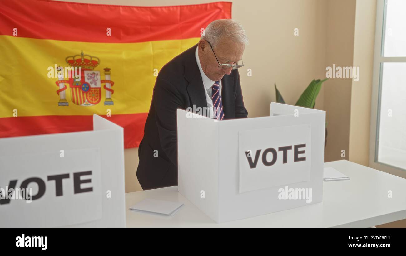Elderly grey-haired man voting in an indoor polling station with a ...