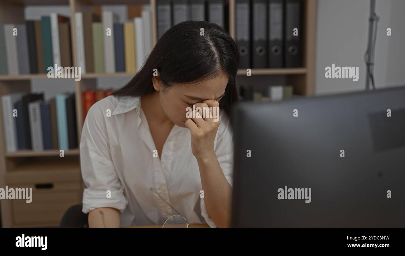 Stressed chinese woman sitting in her office with her hand on her face ...