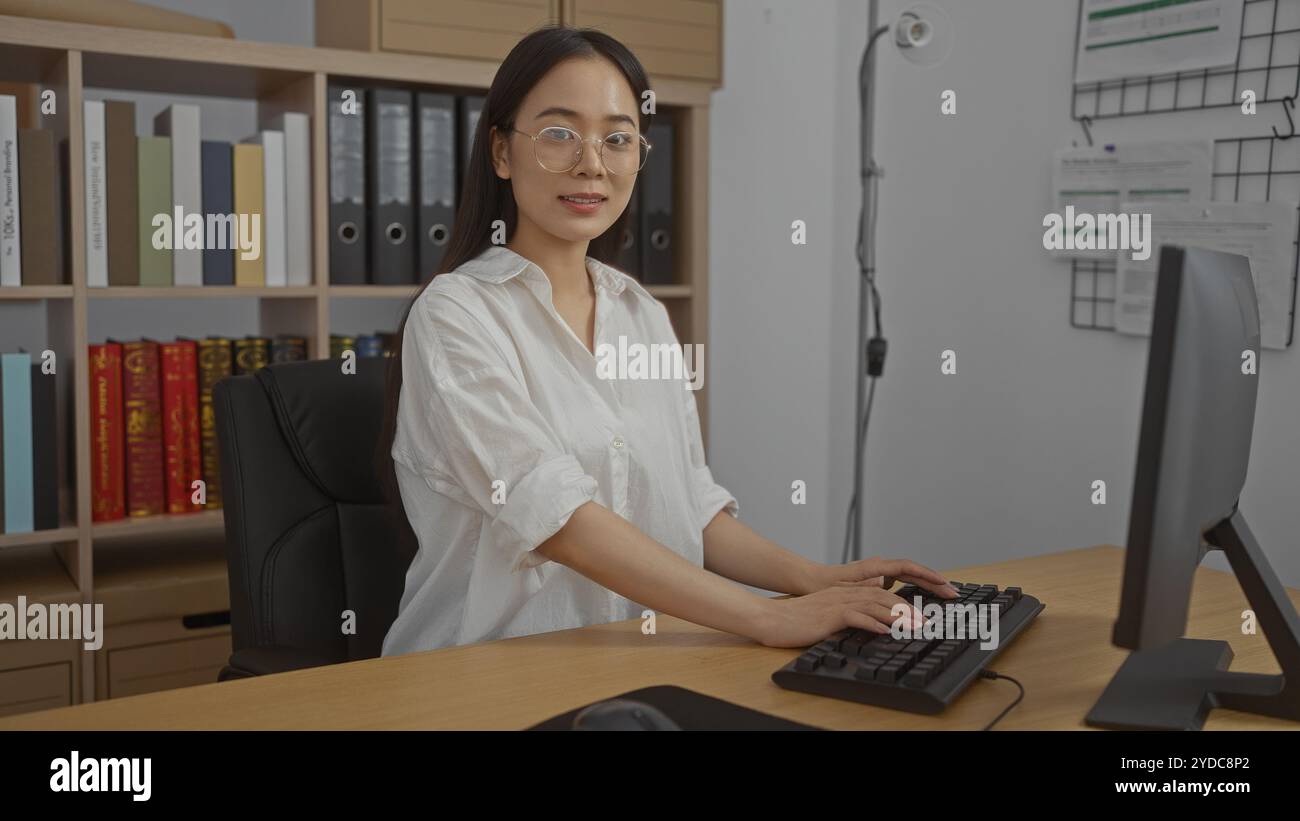 Young chinese woman working on a computer in an office, surrounded by ...