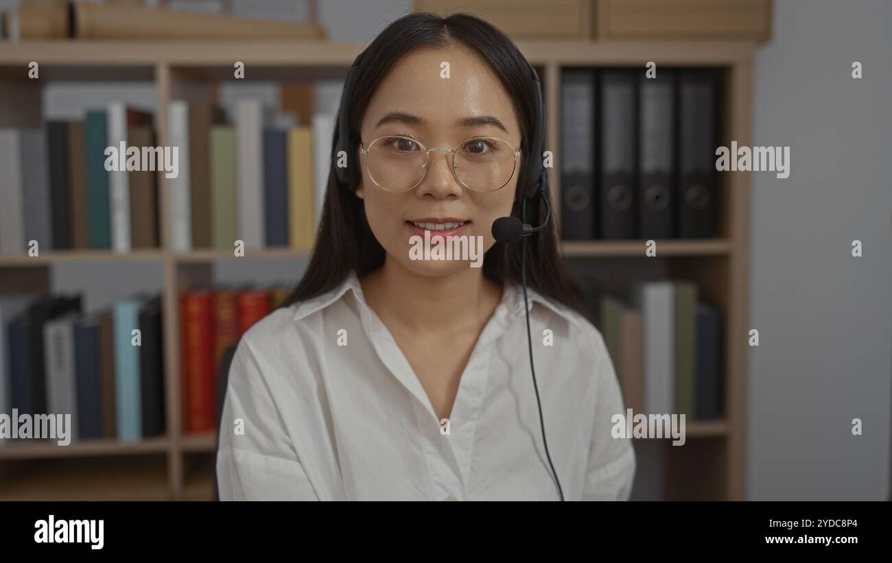 Young chinese woman with glasses and headset smiling in office ...