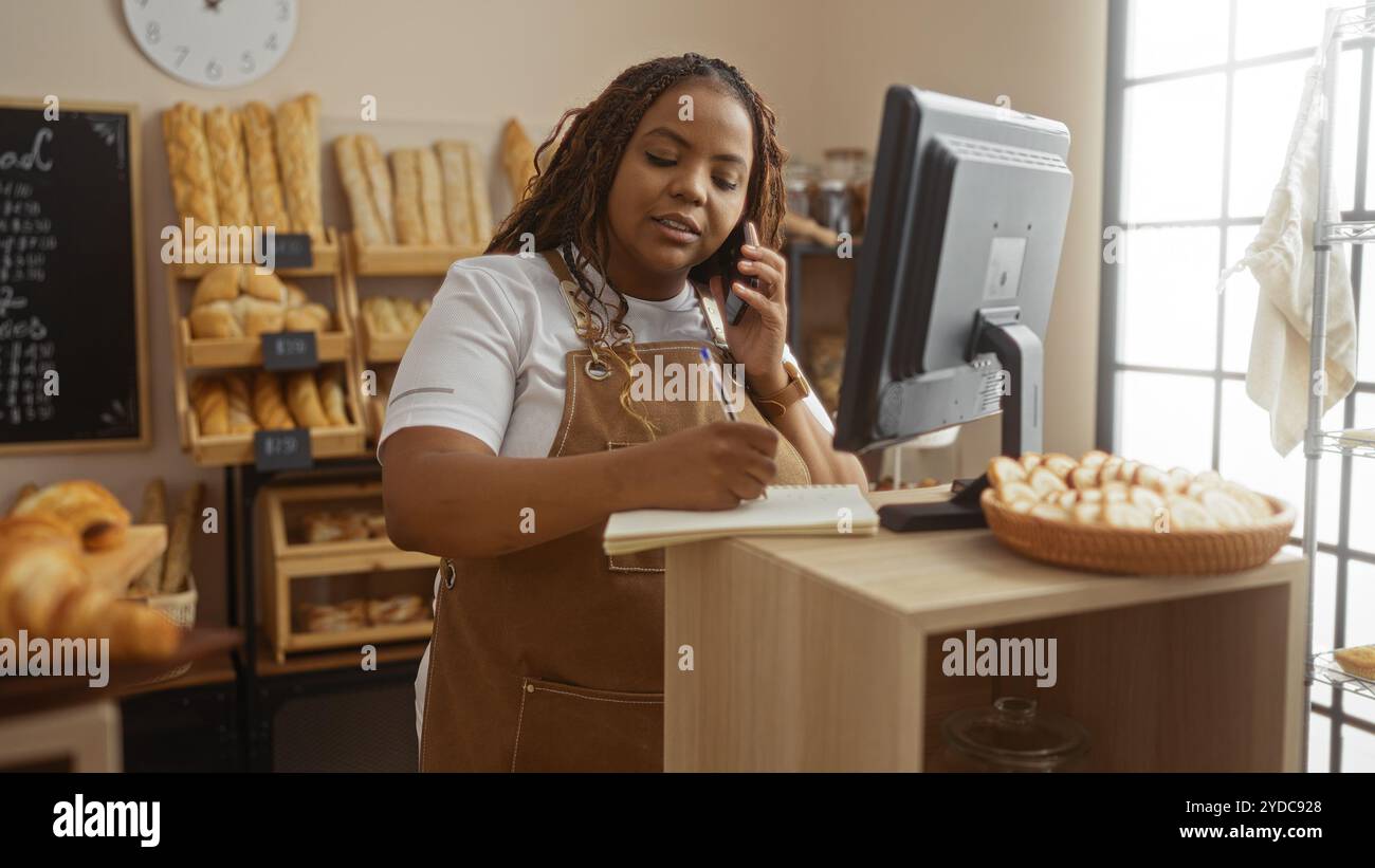 Plus size woman working in a bakery shop, taking notes, and talking on ...