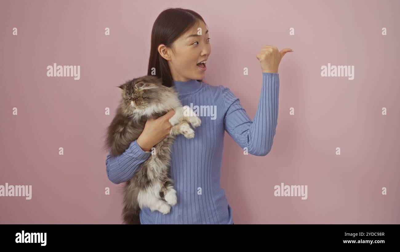 Young asian woman holding a furry cat, pointing to the side with ...