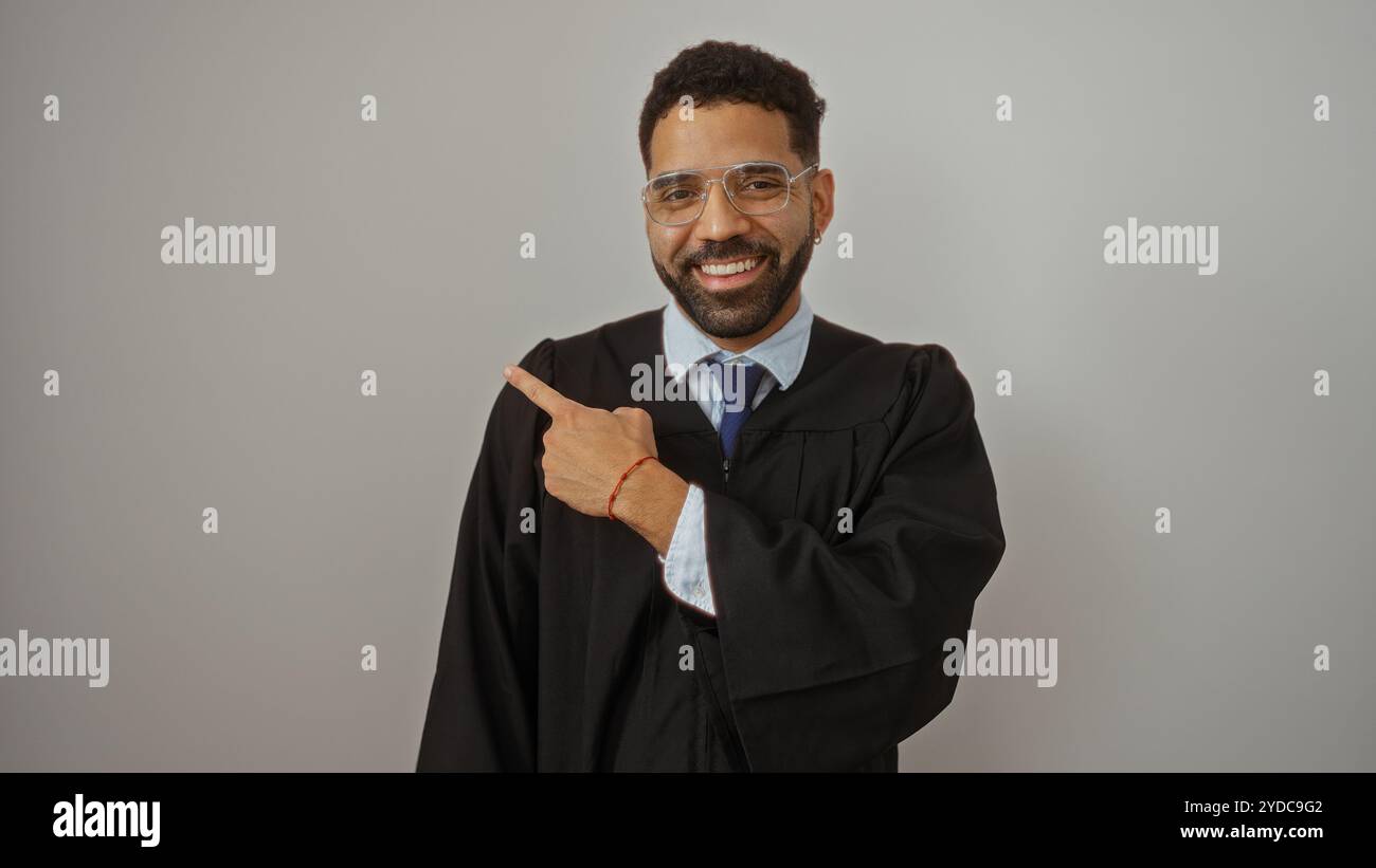Young man in graduation gown with glasses smiling and pointing over ...