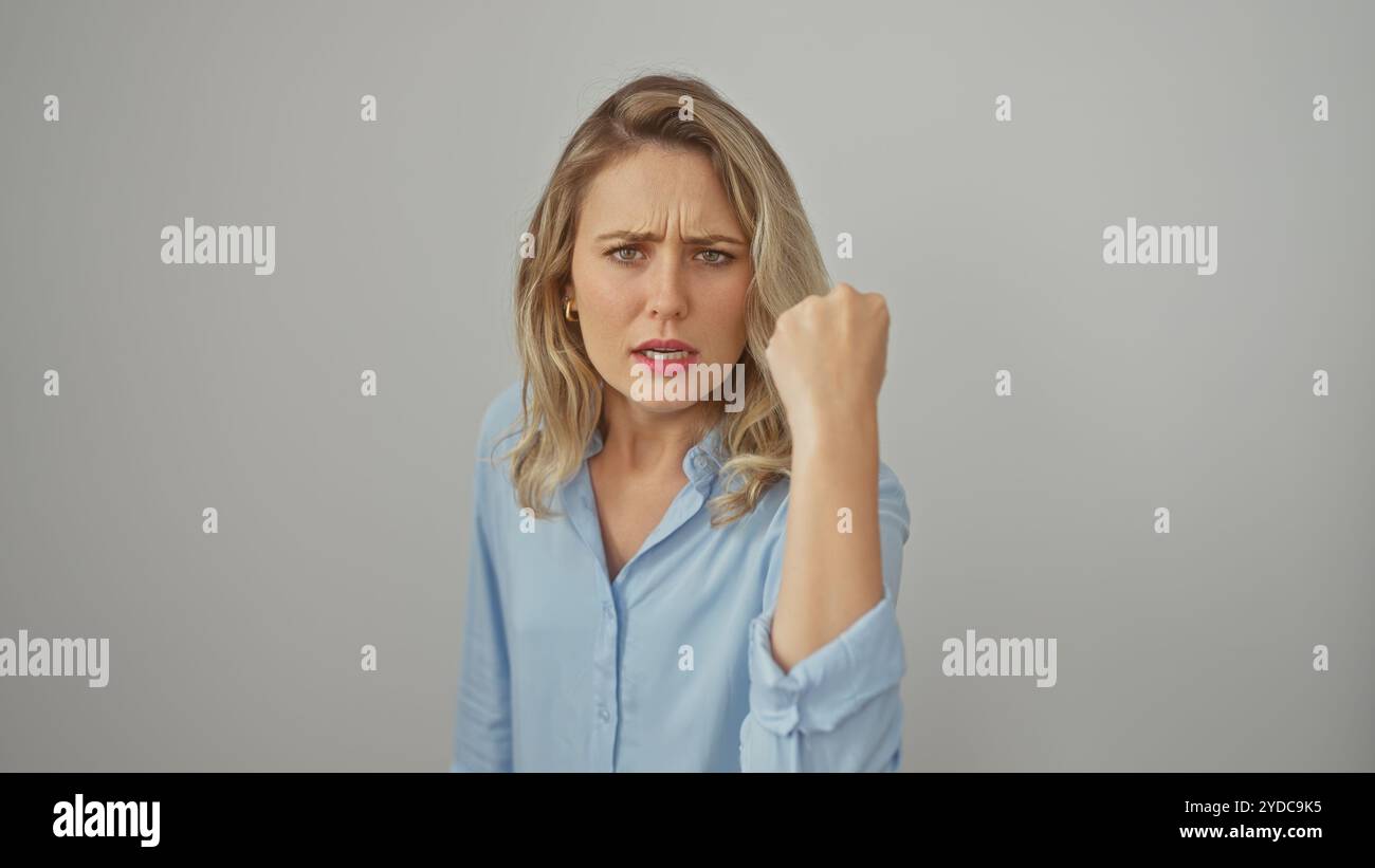 Confused young woman in blue shirt showing fist against a white ...