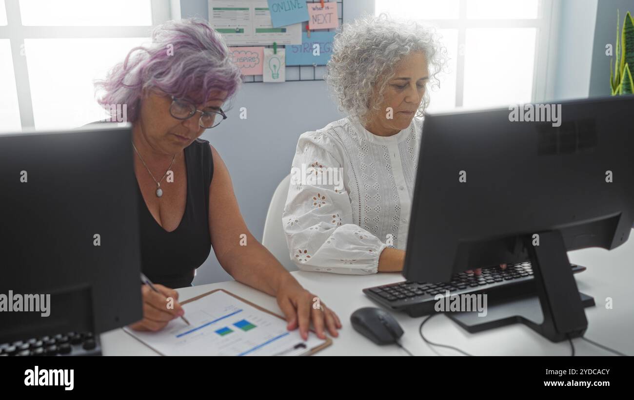 Women collaborating in an office setting, working on computers and ...