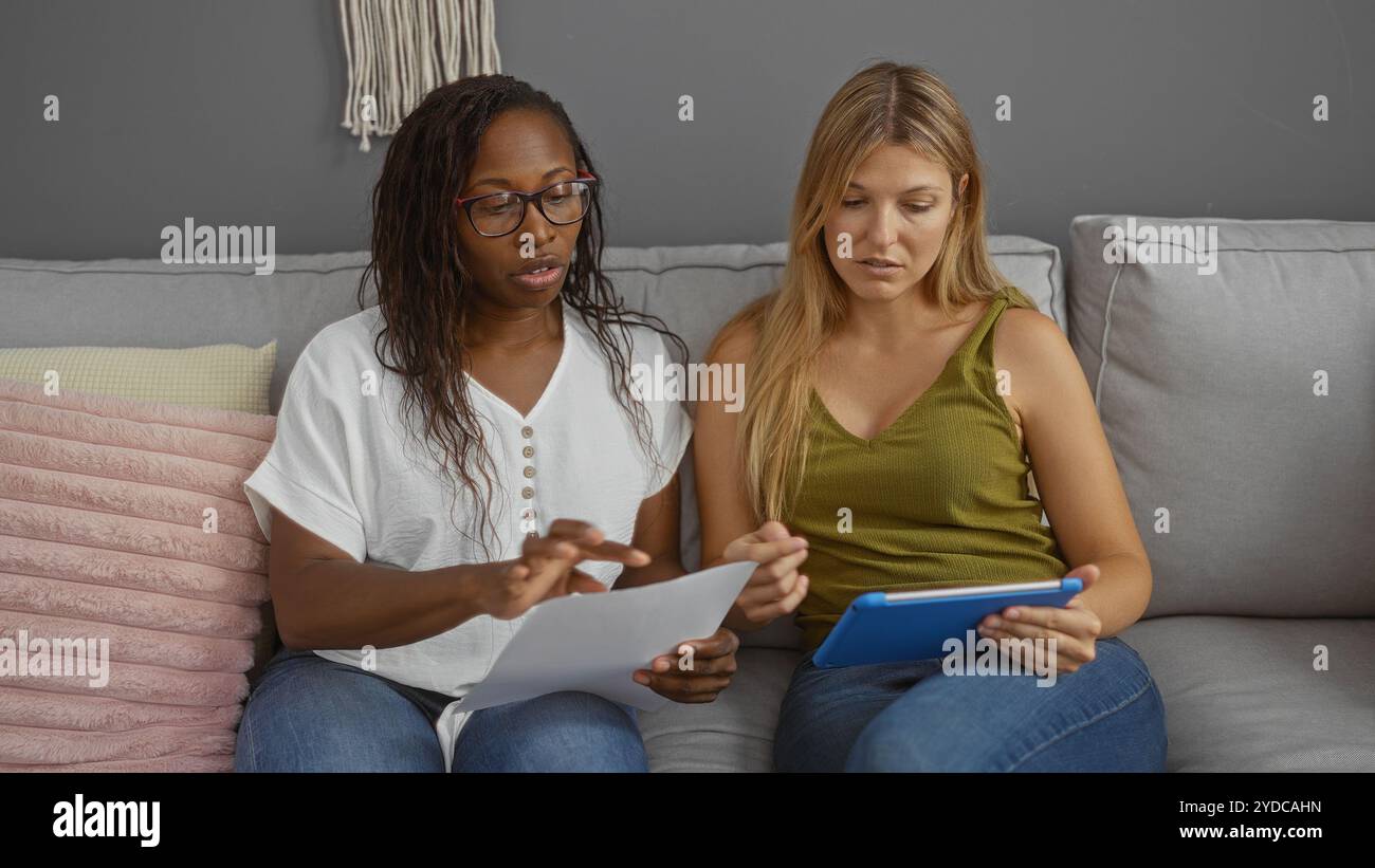 Two women discussing documents on a couch in a cozy living room, one ...