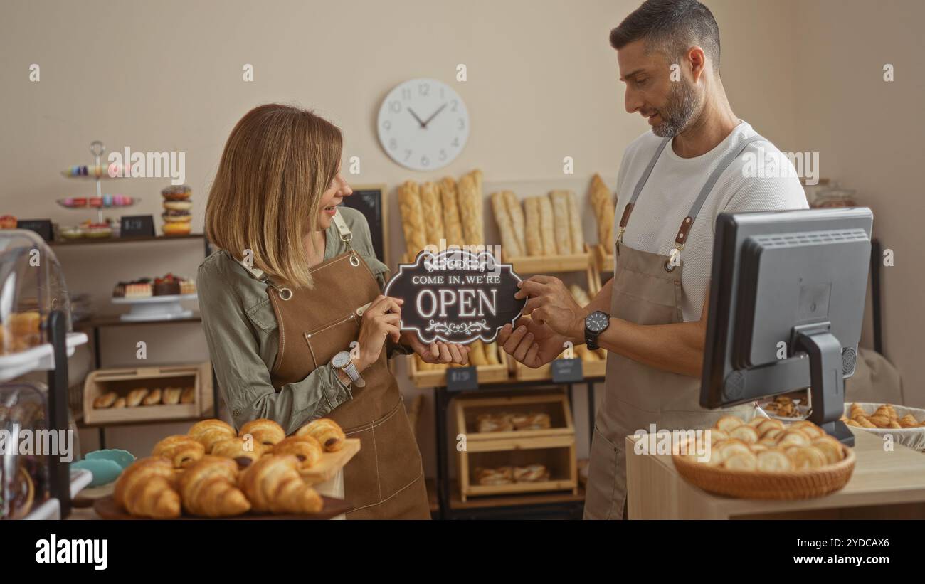 Man and woman workers holding open sign in bakery shop interior with ...