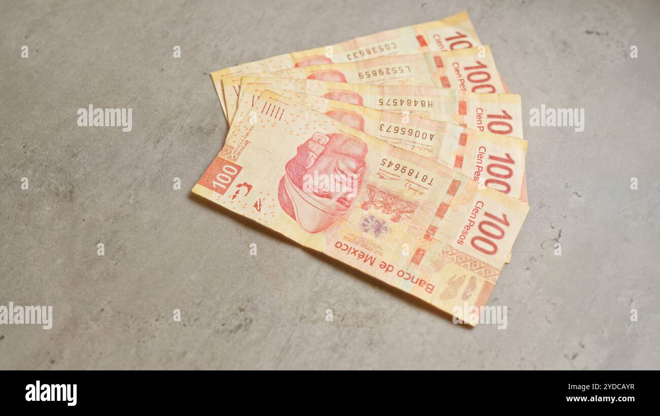Mexican 100 peso banknotes spread on a concrete surface, highlighting ...