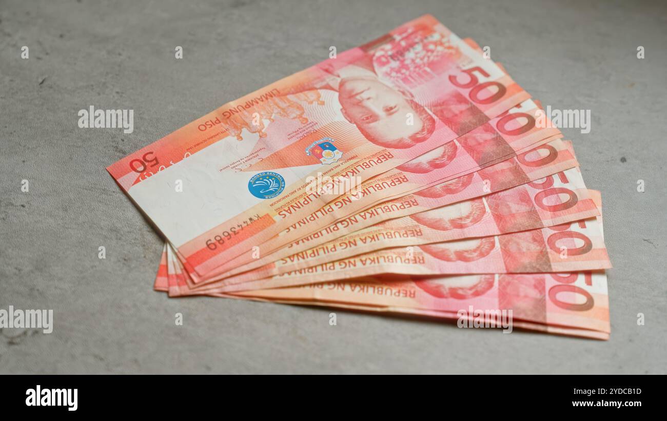 Philippine pesos banknotes are spread out on a concrete surface ...