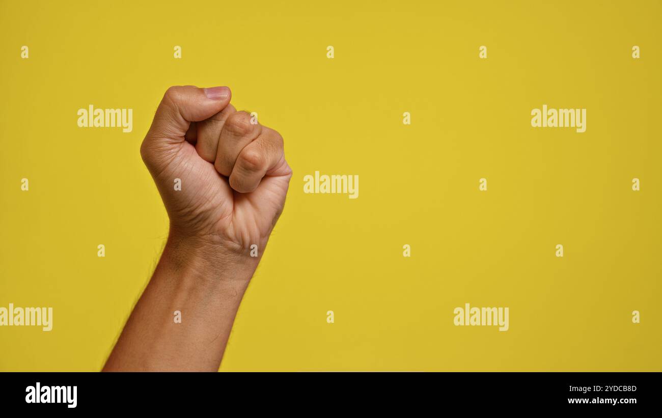 Man's hand making a fist against a vibrant yellow background signifying ...