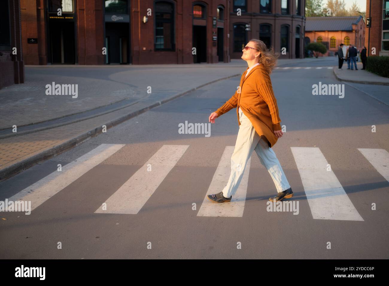 Person in orange cardigan walking on a pedestrian crosswalk in urban ...