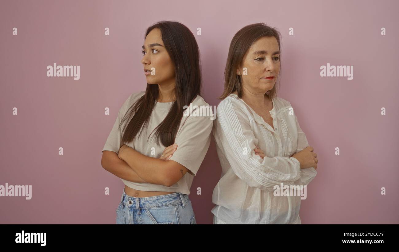 Mother and daughter standing back to back with arms crossed against a ...