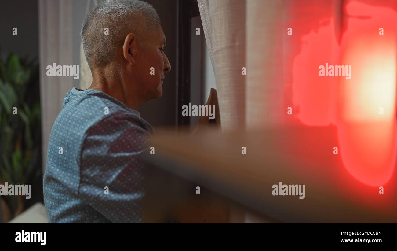 A middle-aged hispanic man with grey hair peeks through curtains inside ...