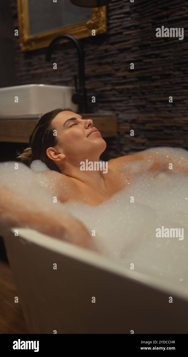 A serene young woman enjoys a luxurious bubble bath in a stylish modern bathroom interior Stock ...