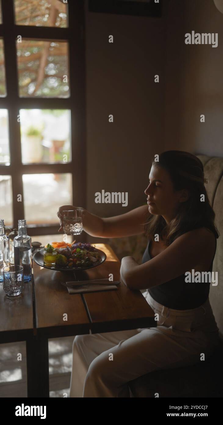 A contemplative young woman sits alone in a dimly lit modern cafe ...