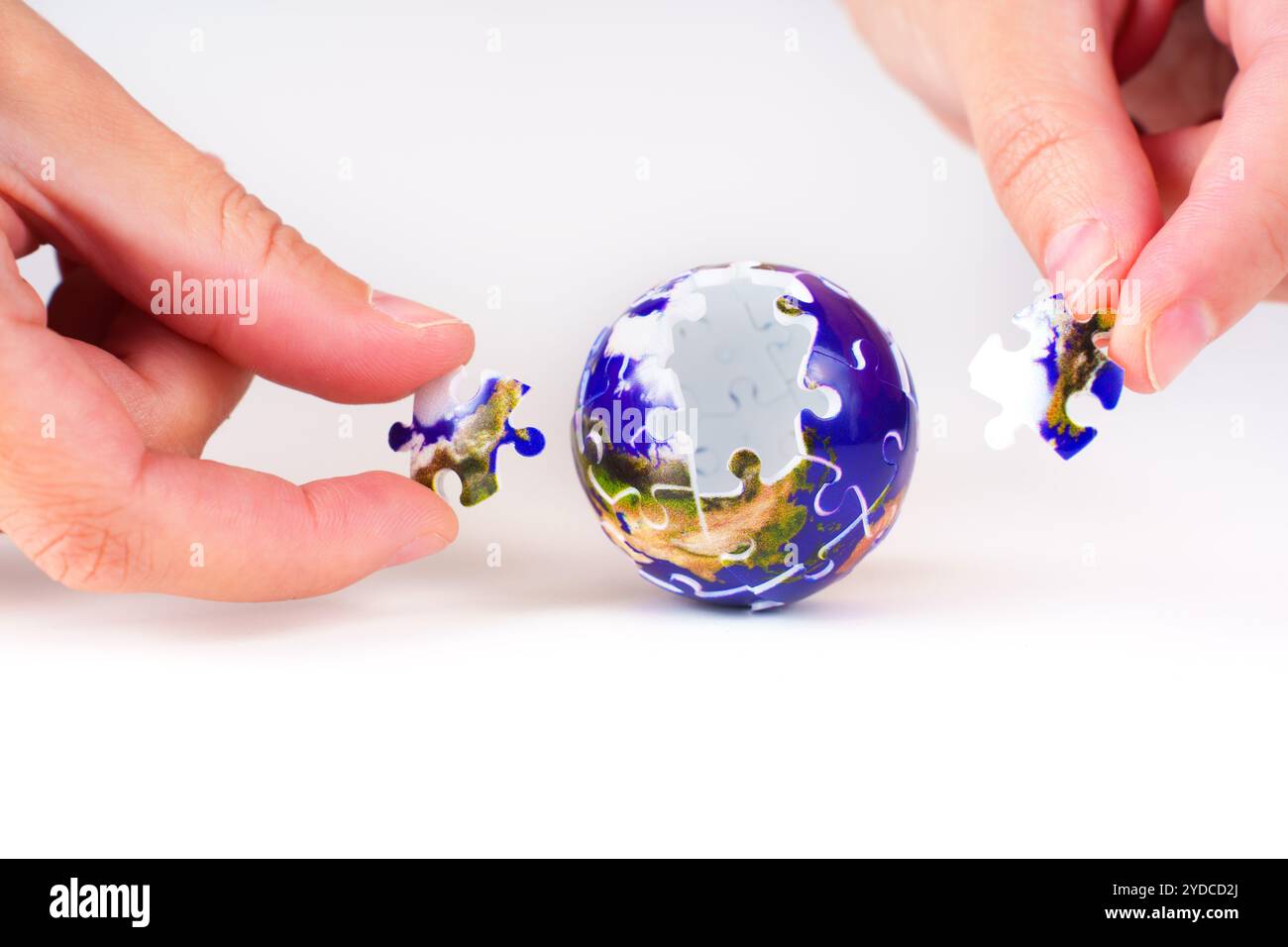 Two hands working on a colorful puzzle globe, symbolizing collaboration and problem-solving ...