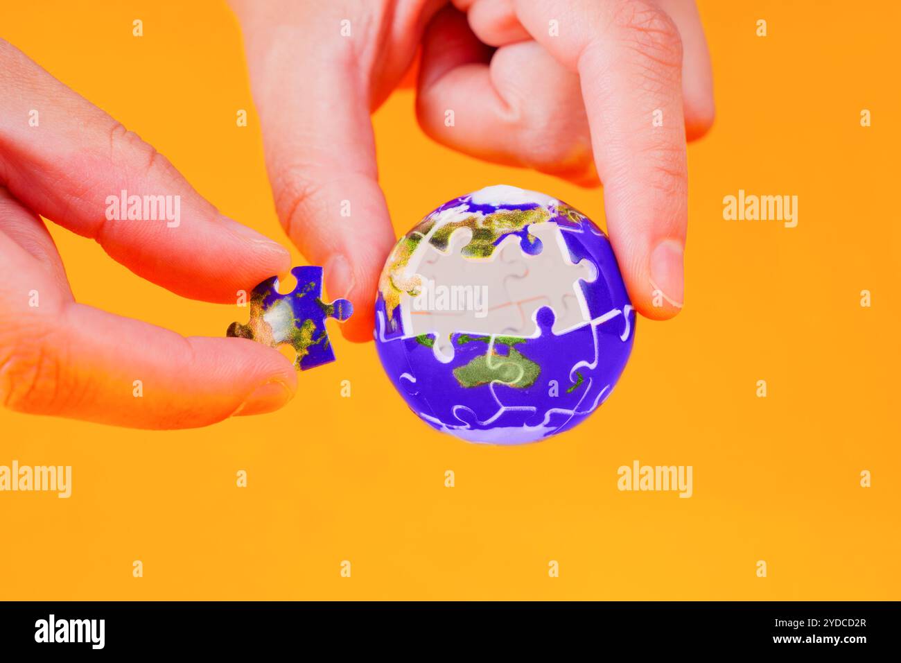 Hands fitting a puzzle piece into an Earth globe set against a vibrant ...