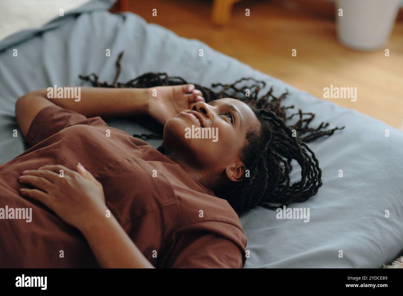 Smiling woman lying comfortably on bed looking relaxed and serene. She ...