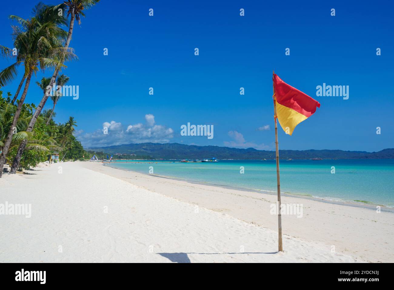 Red and yellow safety flag on a tropical white sand beach with clear ...