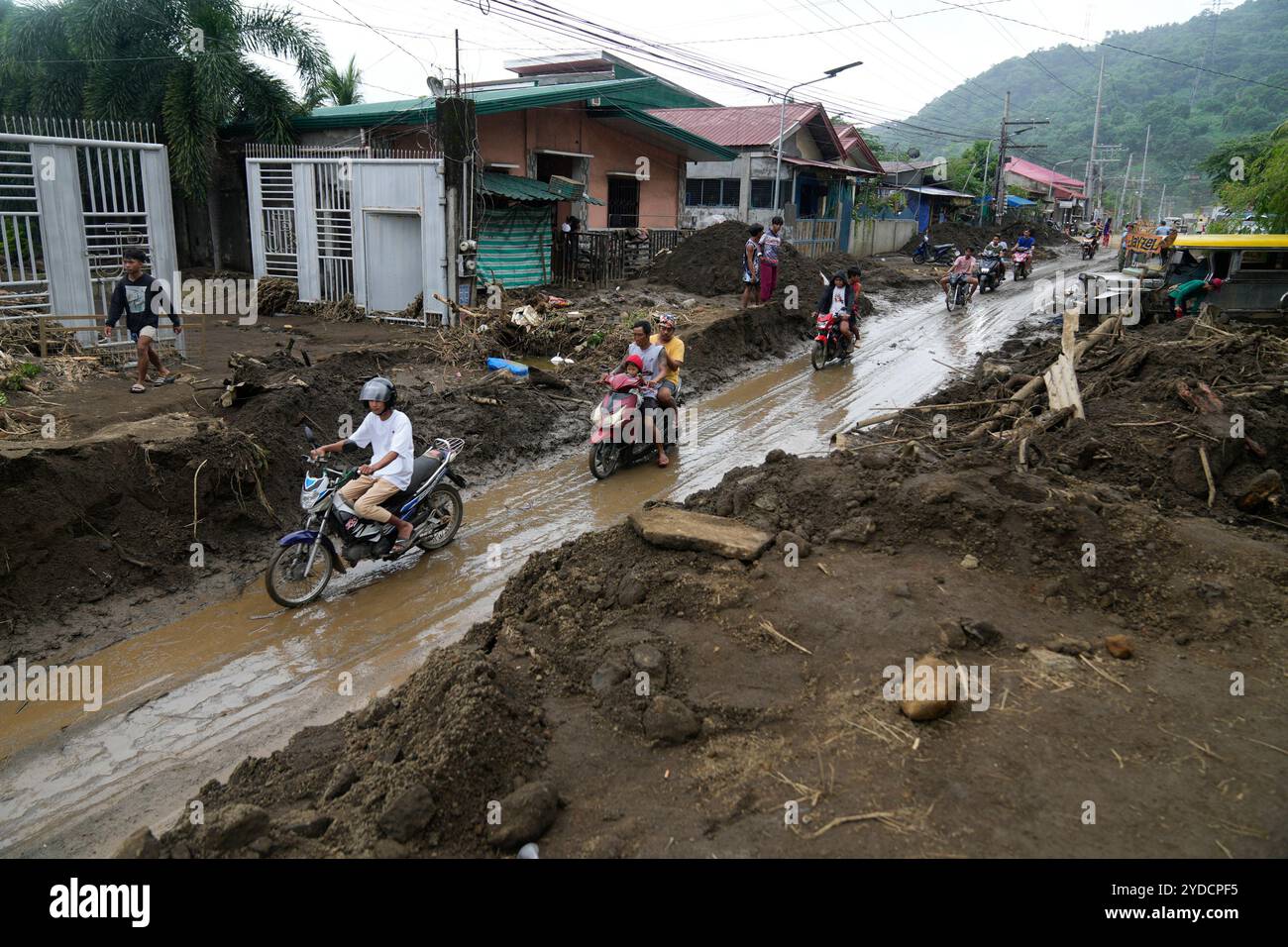 Residents ride motorcycles along a mud covered road after a landslide ...
