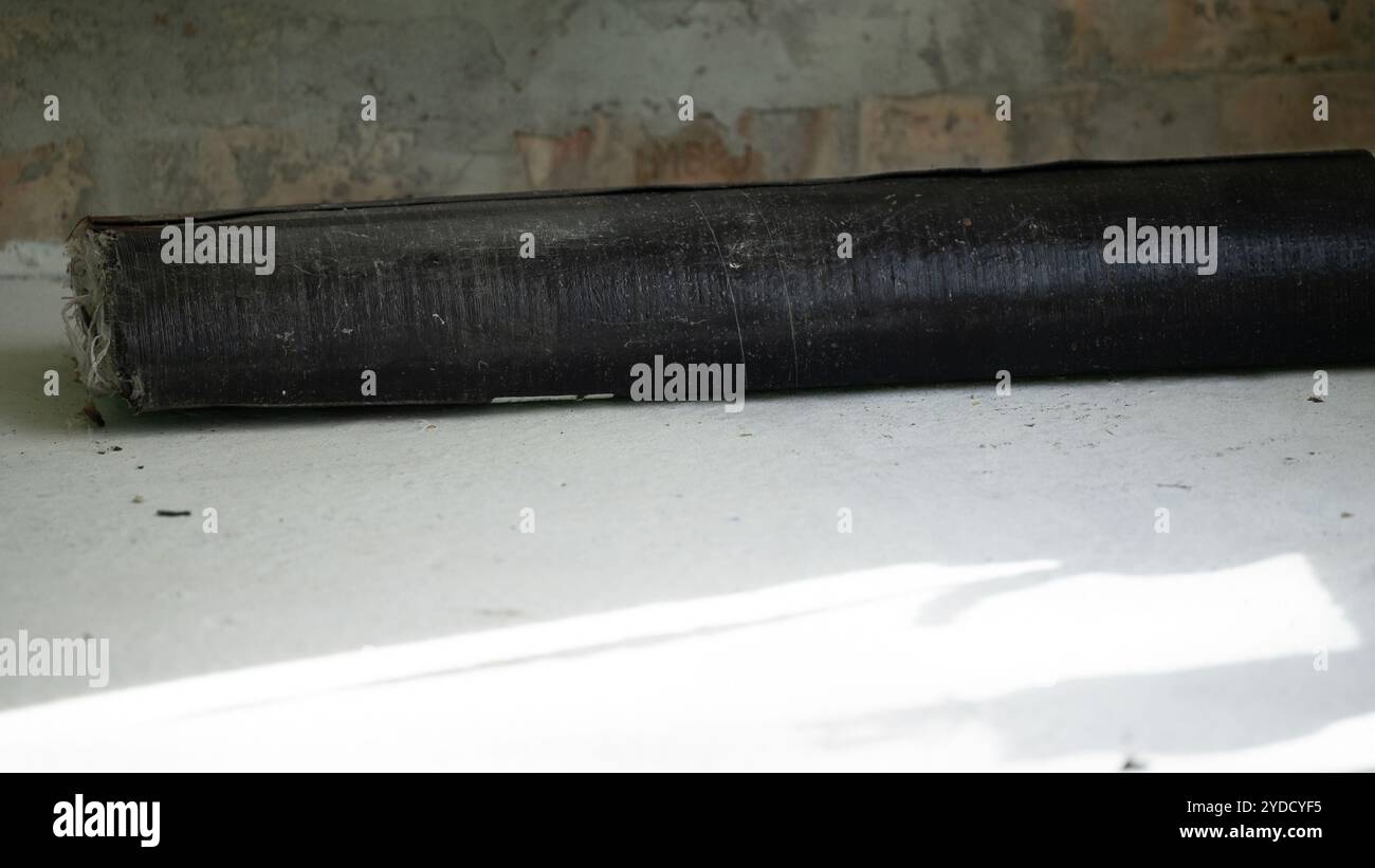 A roll of bitumen roofing material lies on a concrete floor ...