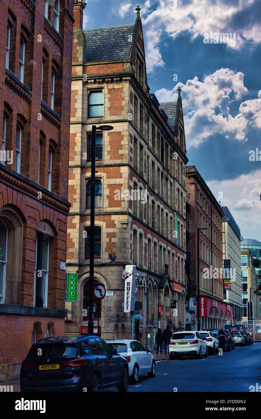 A city street with brick buildings, parked cars, and a cloudy sky. The ...