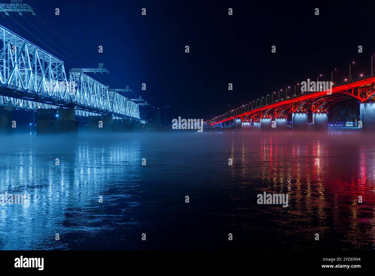 Two illuminated bridges, one blue and one red, stretch over a river at ...