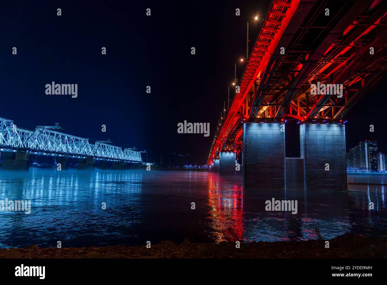 Red and blue illuminated bridges stretch over a river at night, with ...