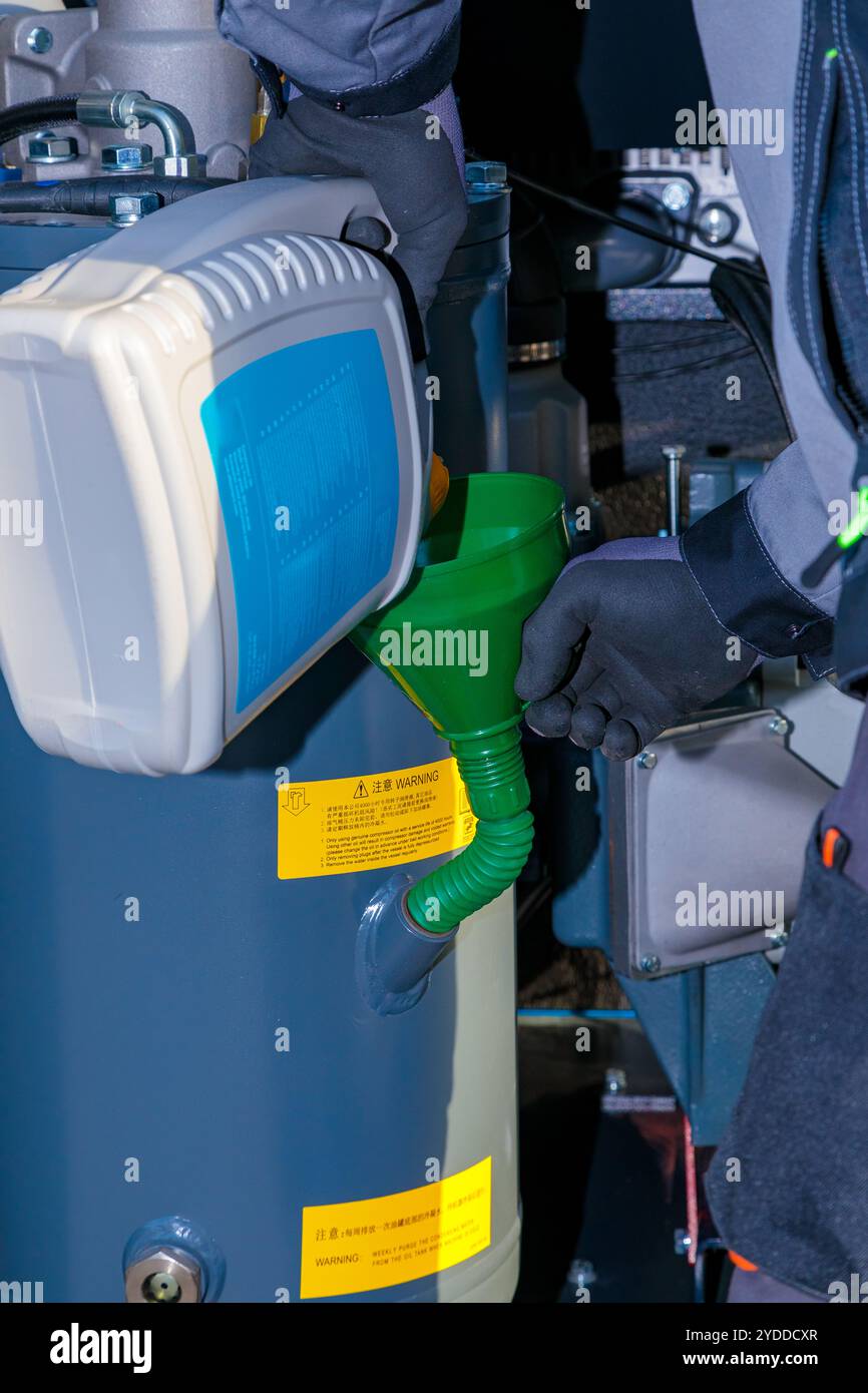 Close-up of a technician pouring oil into an industrial compressor ...