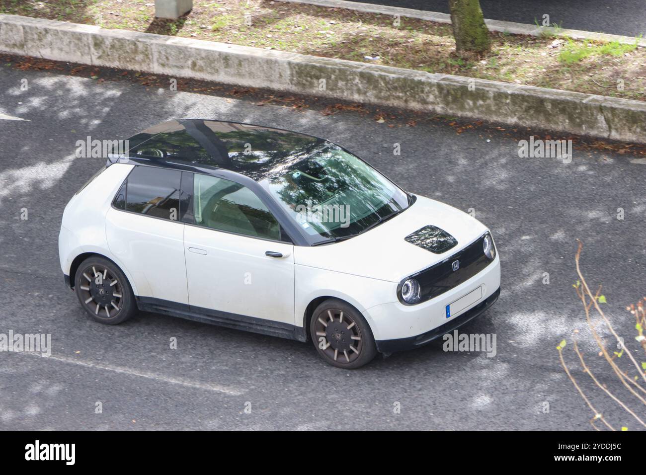 White honda e electric car driving on a road, passing by a sidewalk ...