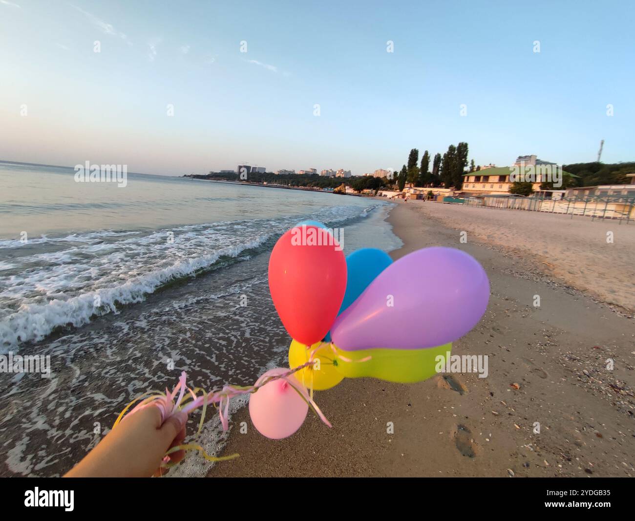 Hand and many colorful balloons tied with a ribbon near the sea on the ...