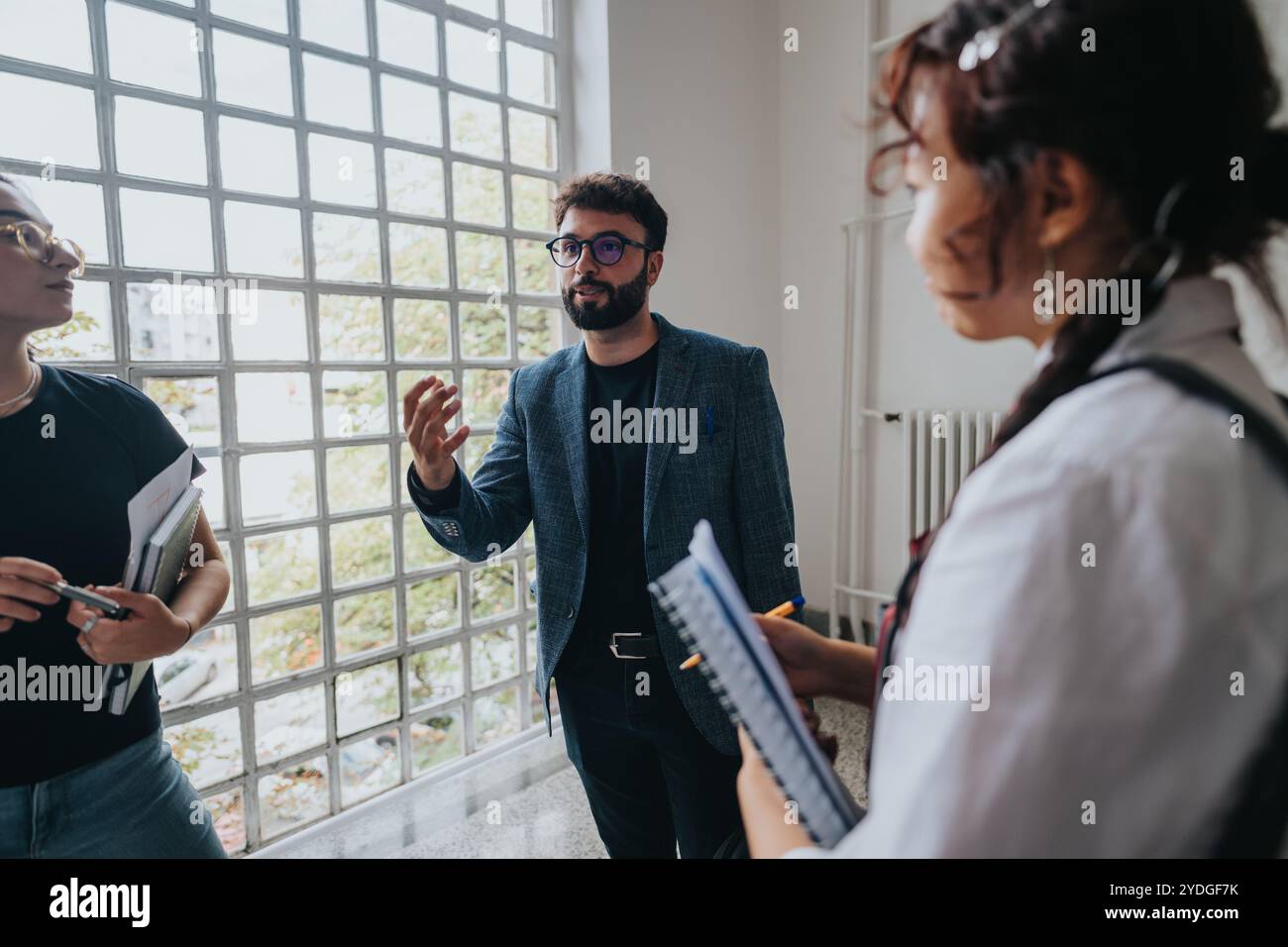 University professor engaging with students in a bright, open hallway Stock Photo - Alamy