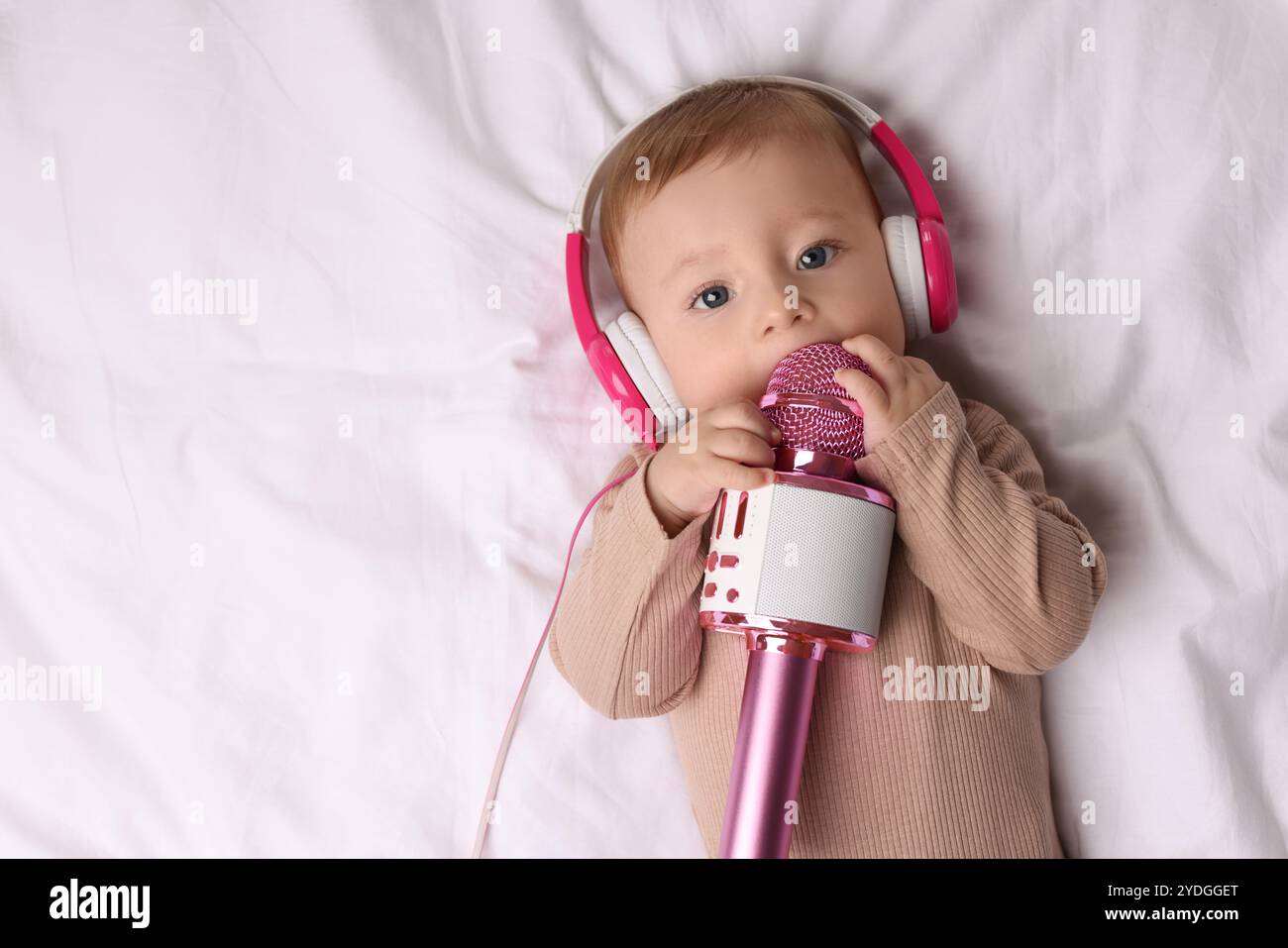 Cute little baby with headphones and microphone lying on bed, top view ...