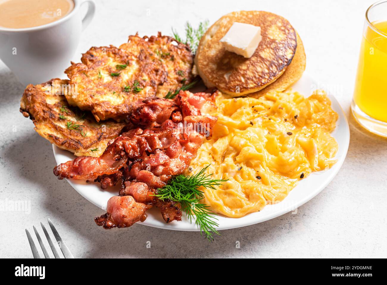 Full American Breakfast with scrambled eggs, fried bacon, hash browns and pancakes on plate ...