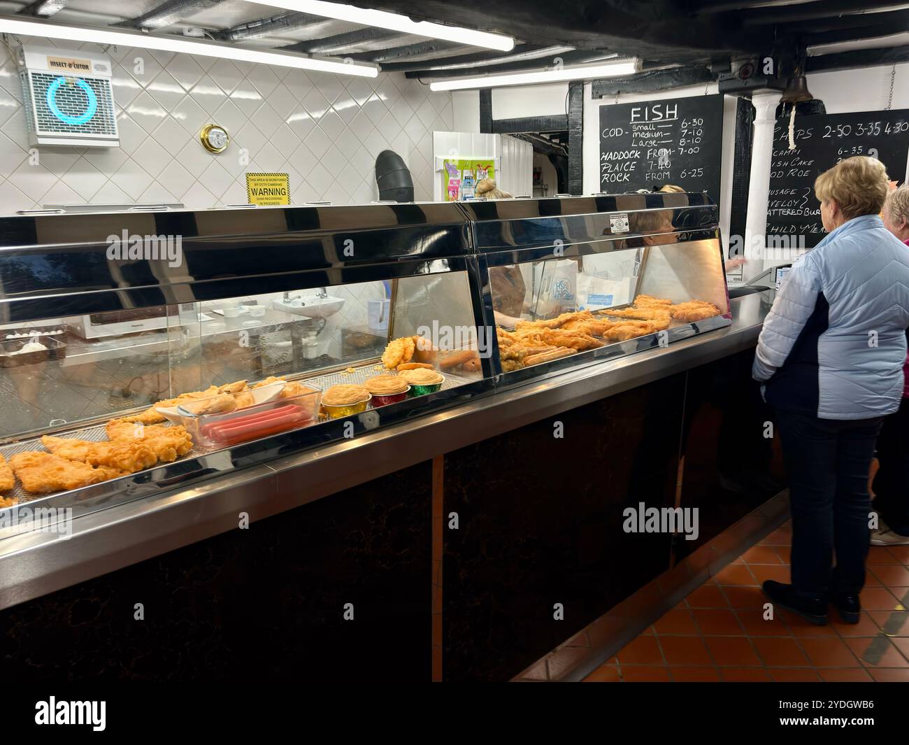 Customer inside traditional fish and chip shop with battered fried food ...