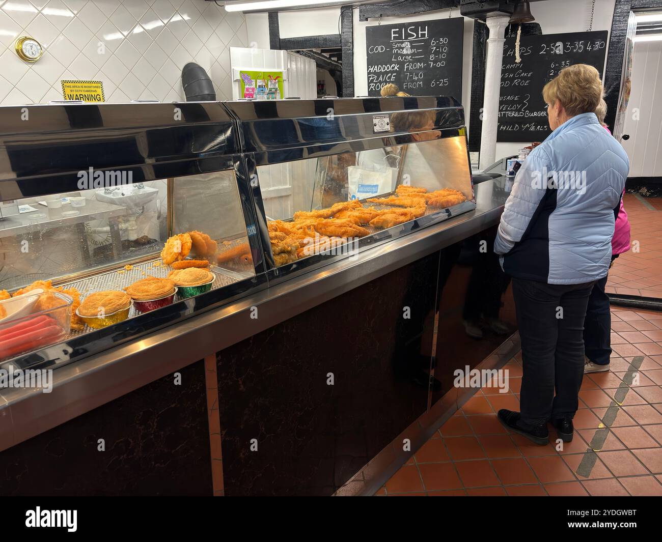 Customer inside traditional fish and chip shop with battered fried food ...