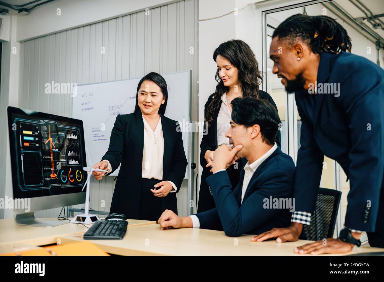 A diverse group of professionals in a meeting, surrounding a desktop ...