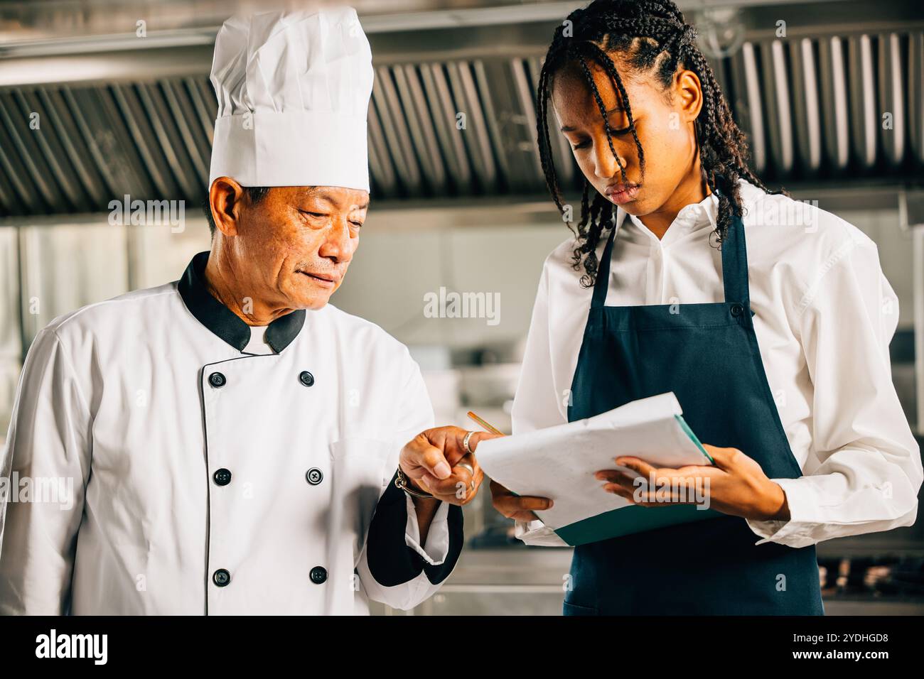 In a restaurant kitchen an Asian senior chef educates multiracial ...