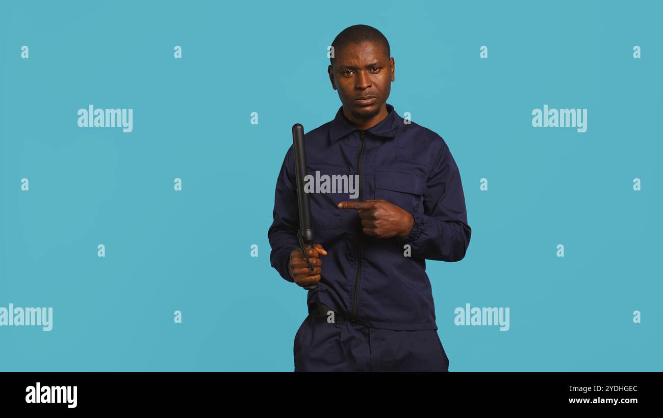 Portrait of security guard removing cane from belt while overseeing ...