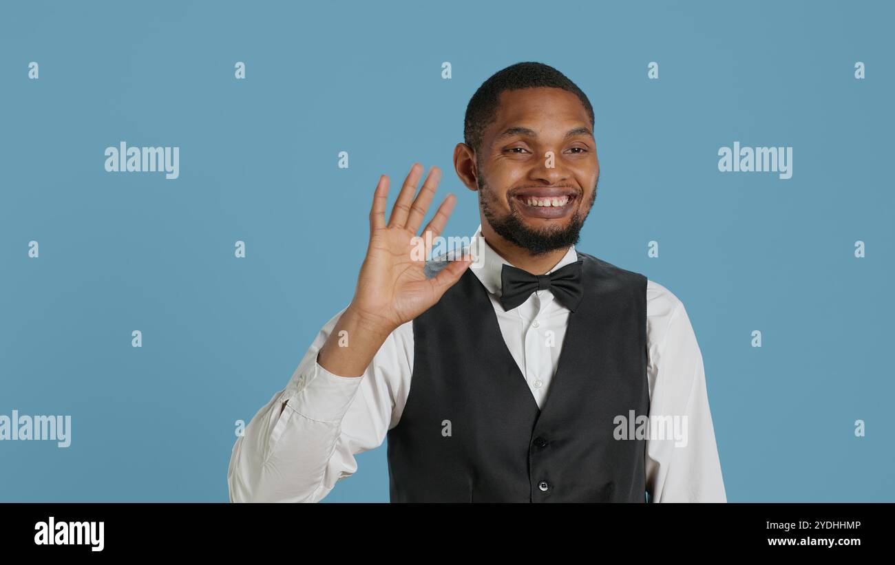Bellboy employee smiling and waving hello at hotel guests, greeting ...