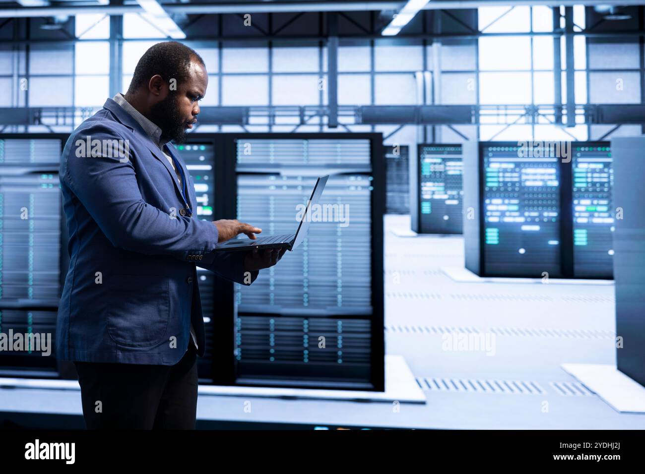 Computer scientist walking in data center, using laptop to configure network infrastructure such ...