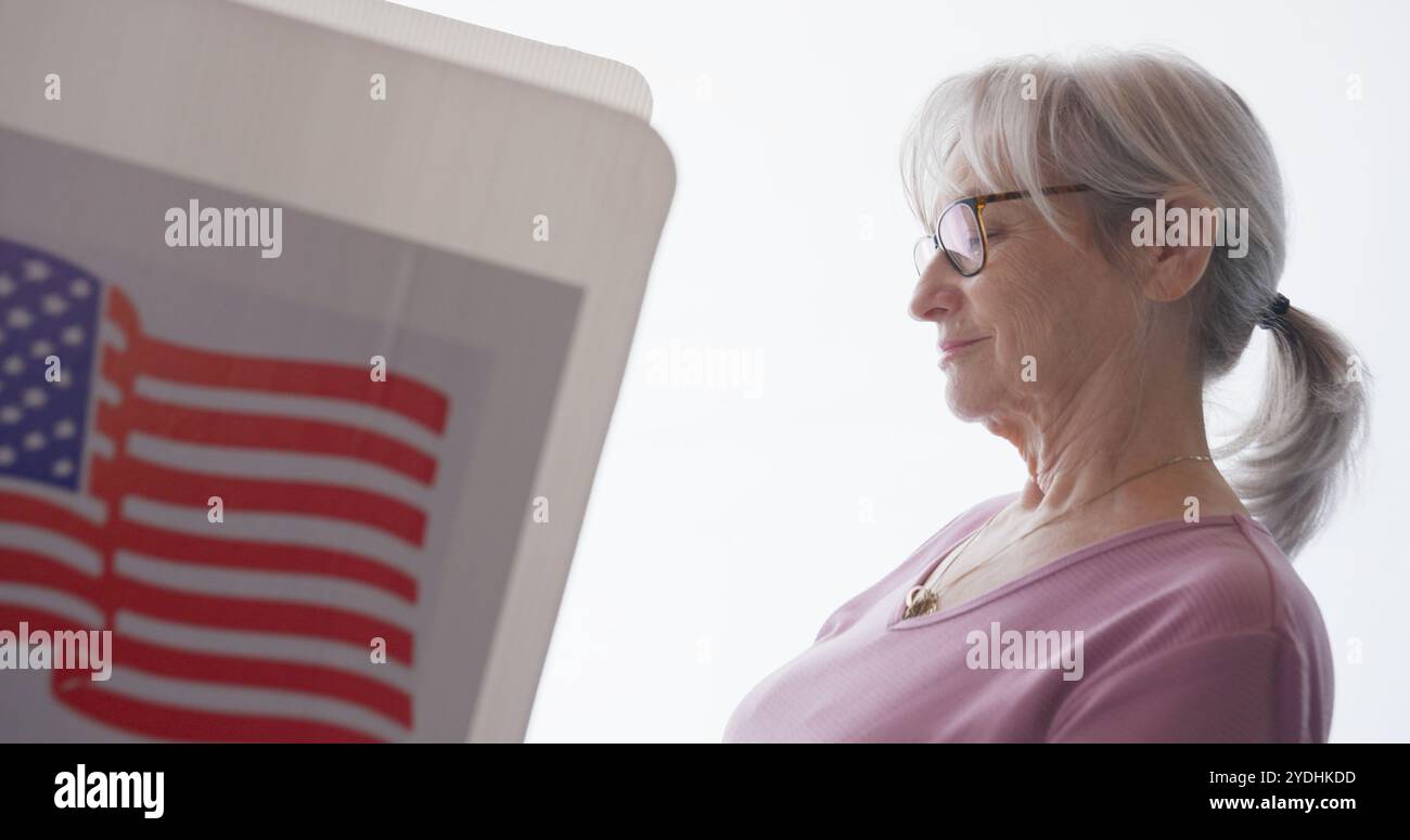 Senior woman casts votes at booth with white background behind. Close ...
